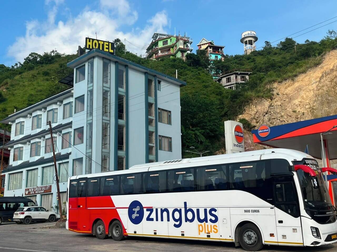 Um ônibus com a marca 'zingbus plus' estacionado em frente a um hotel.