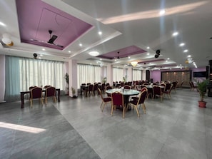 Uma sala de conferências espaçosa com mesas e cadeiras redondas, ventiladores de teto e iluminação embutida.