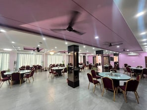 Sala de conferência com várias mesas e cadeiras, ventiladores de teto e iluminação embutida.