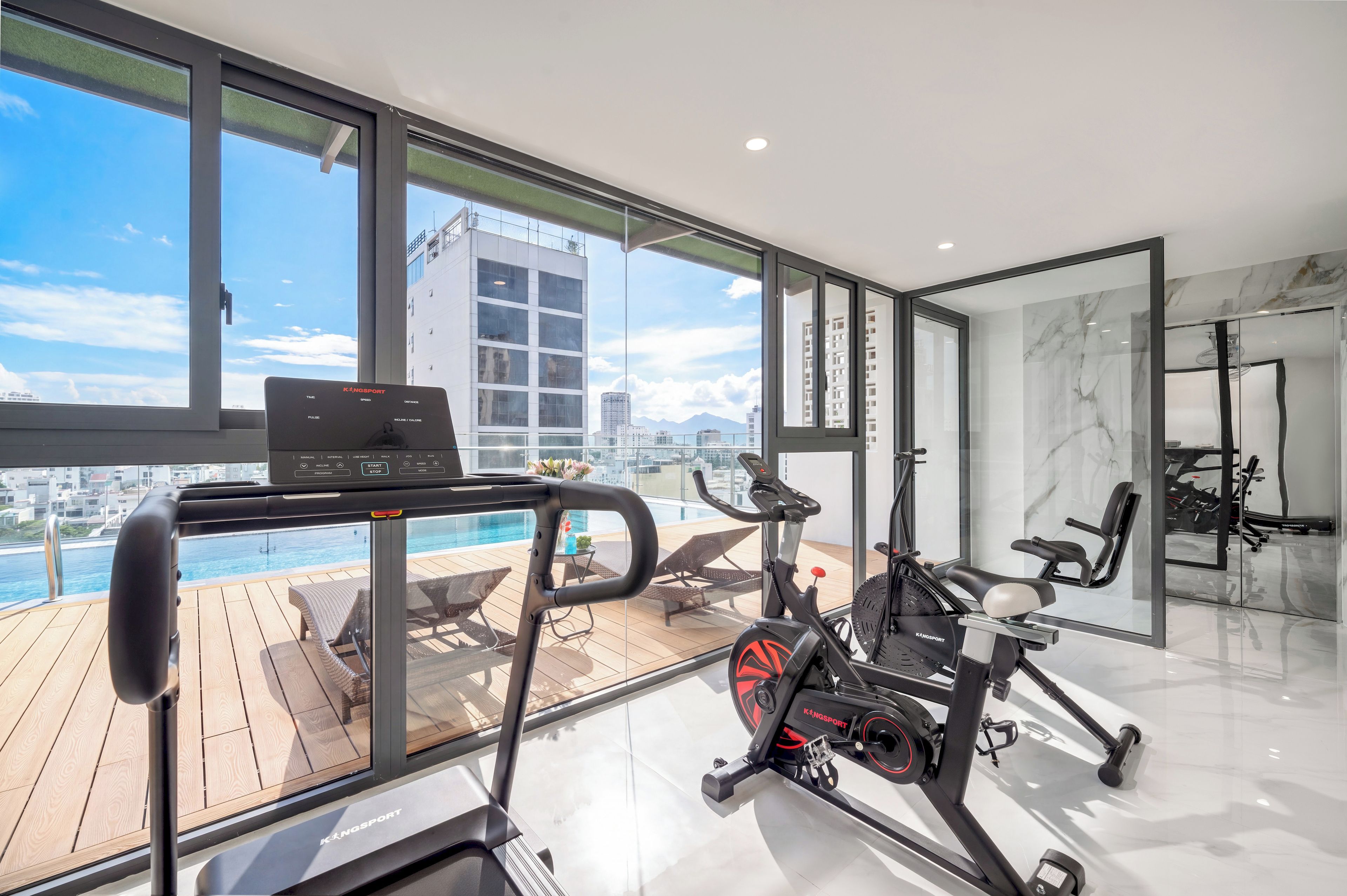 Academia moderna com equipamentos de ginástica, área de piscina e vista para a cidade.
