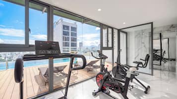 Academia moderna com equipamentos de ginástica, área de piscina e vista para a cidade.