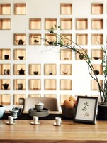 Quarto com mesa de madeira, conjunto de chá, quadro emoldurado e prateleiras com diversos objetos.