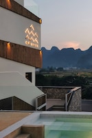Um hotel moderno com piscina, vista para montanhas e um letreiro com letras iluminadas.