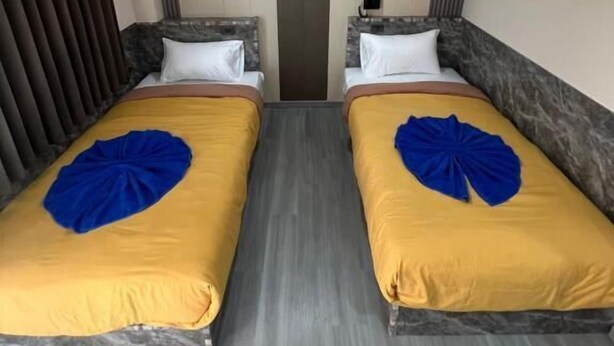 Quarto de hotel com duas camas, cada uma com cabeceira e travesseiro, e um lustre central.