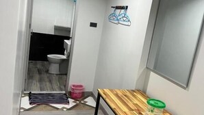 Um banheiro pequeno com vaso sanitário, espelho e uma mesa de madeira com um banquinho.