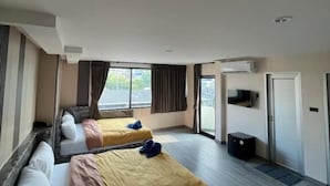 Quarto de hotel com duas camas, uma janela grande, uma porta e uma pequena escrivaninha.