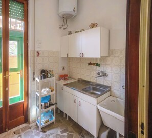 Cozinha compacta com armários brancos, pia de aço inoxidável e painel de azulejos.