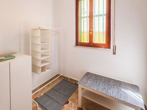 Quarto pequeno e limpo, com um banco, prateleira suspensa e janela com vista.