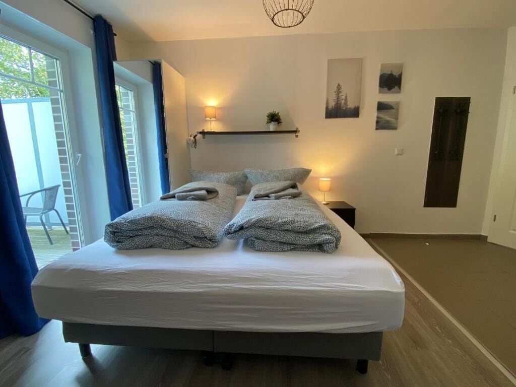 Quarto com cama, luminárias de cabeceira, um armário com uma planta e uma porta.