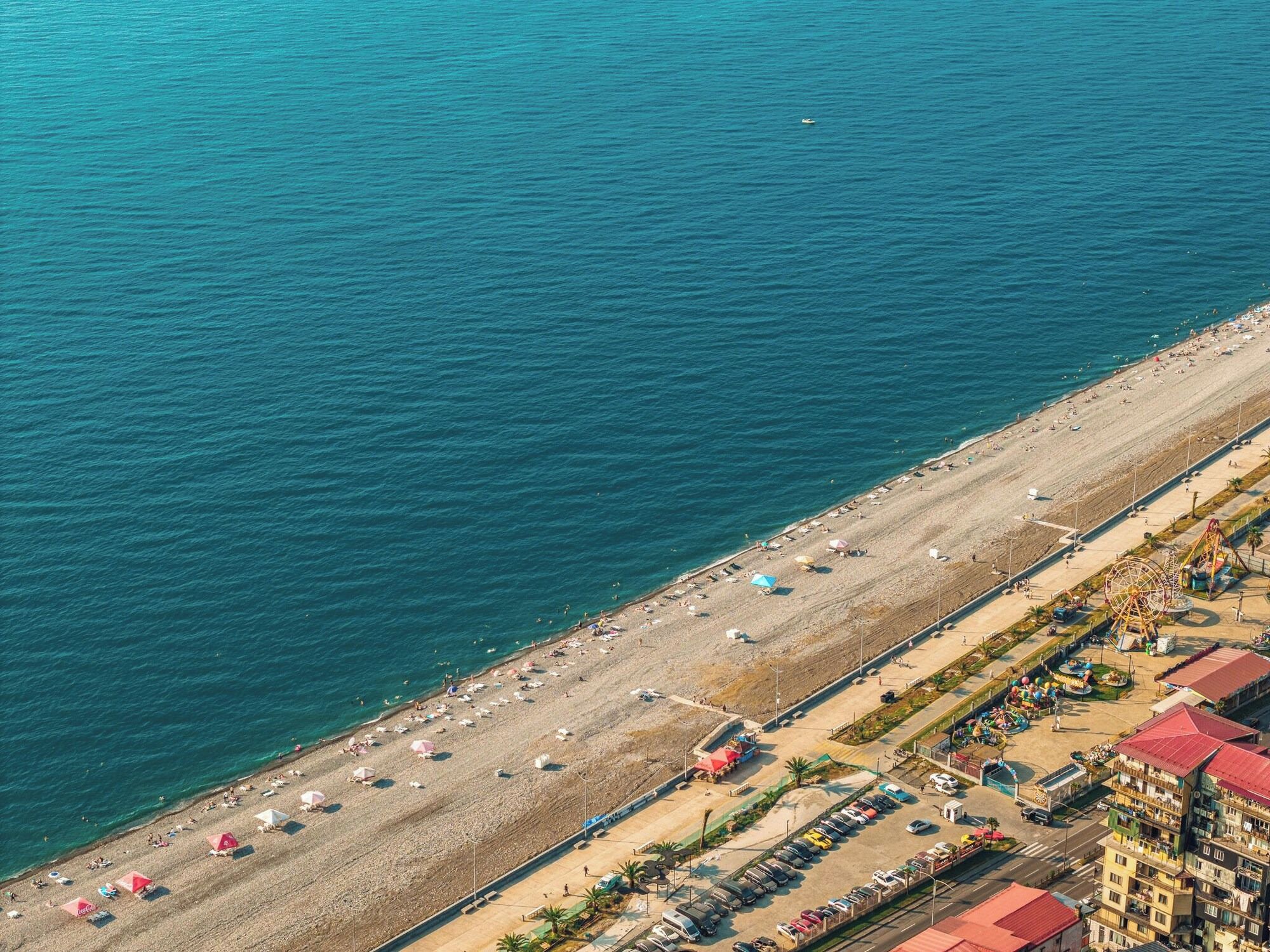 Vista aérea de uma praia com uma fileira de guarda-sóis, um estacionamento e uma roda gigante.