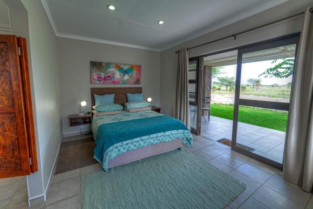Quarto com cama, mesa de cabeceira, quadro e vista para uma área gramada pela porta deslizante.