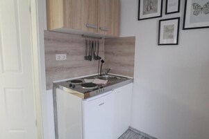 Cozinha compacta com fogão embutido, armários brancos e suporte para utensílios fixado na parede.