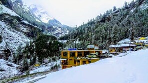 Uma área montanhosa coberta de neve com um edifício amarelo que parece ser uma pousada ou hotel.