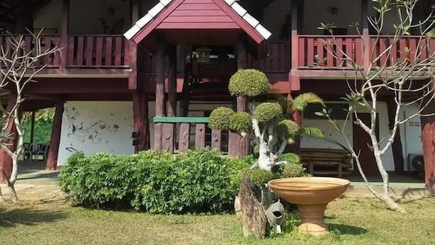 Um edifício de dois andares com varanda, alpendre e um jardim bem cuidado.