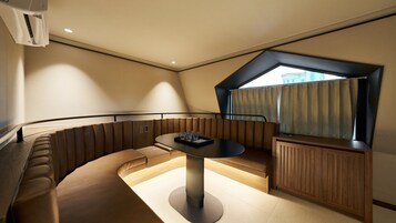 Um interior moderno com uma área de estar em curva, uma mesa central e uma janela ampla com cortinas.