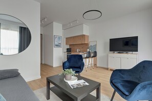 Uma sala de estar moderna com um sofá, duas poltronas, uma mesa de centro com uma revista e uma televisão em um gabinete.