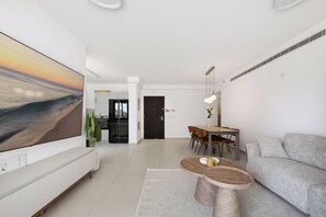 Uma sala de estar moderna com televisão de tela plana, sofá, mesa de jantar com cadeiras e cozinha ao fundo.