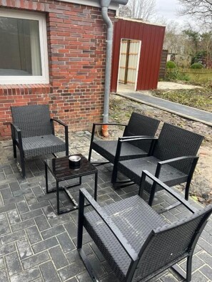Um pátio externo com parede de tijolos, uma porta vermelha e uma mesa de metal com quatro cadeiras.