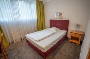 Quarto de hotel com cama, mesa de cabeceira, cadeira e janela com cortinas.