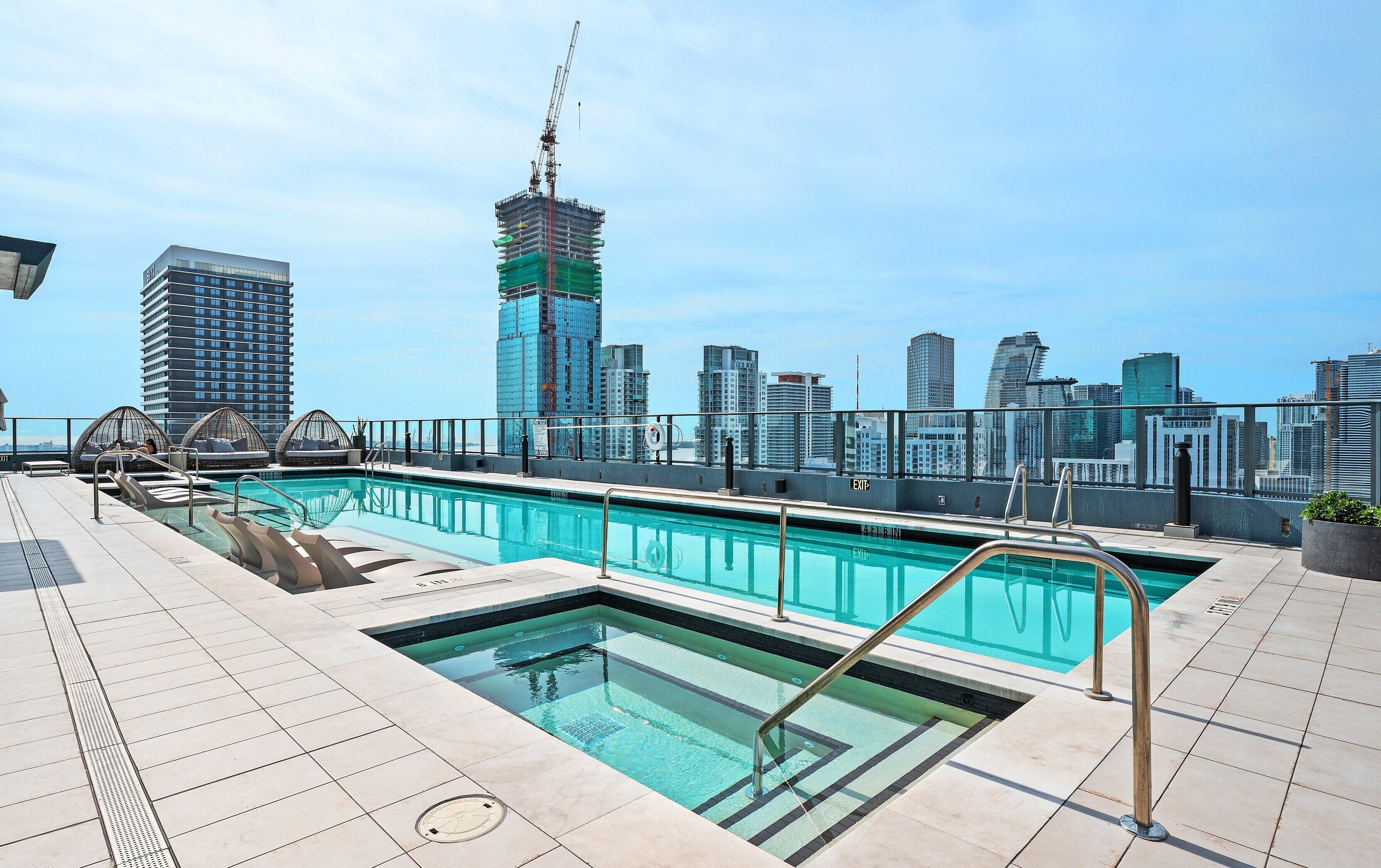 Piscina no terraço com paisagem urbana ao fundo, incluindo um prédio alto em construção.