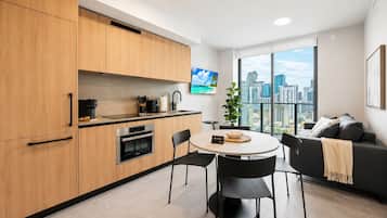 Cozinha moderna com armários de madeira, área de jantar com mesa redonda e vista para a cidade através de grandes janelas.