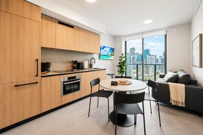Cozinha moderna com armários de madeira, área de jantar com mesa redonda e vista para a cidade através de grandes janelas.