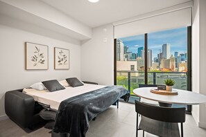 Quarto moderno com cama, sofá, mesa de jantar e vista para a cidade.