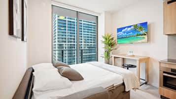 Quarto de hotel moderno com uma cama grande, uma escrivaninha, uma televisão e vista para um edifício alto.