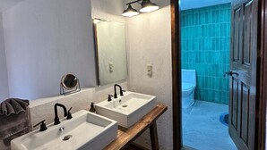 Casa de banho com duas pias, um espelho e uma porta para a área do chuveiro.