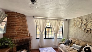 Uma sala de estar acolhedora com lareira de tijolos, um sofá, duas poltronas de vime e uma mesa de centro.
