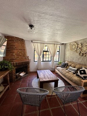 Uma sala de estar aconchegante com lareira de tijolos, um sofá, duas poltronas de vime e uma mesa de centro.