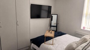 Quarto com cama, televisão na parede, guarda-roupa e mesa de cabeceira com copos.