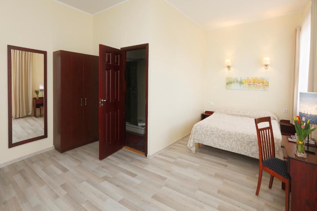 Quarto de hotel com cama, escrivaninha, cadeira, guarda-roupa e espelho.