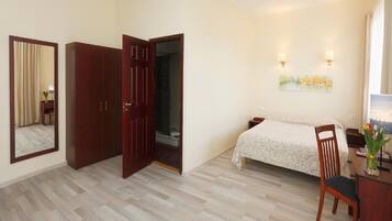 Quarto de hotel com cama, escrivaninha, cadeira, guarda-roupa e espelho.