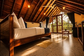 Quarto espaçoso com uma cama grande, teto de madeira e vista através de uma porta de vidro.