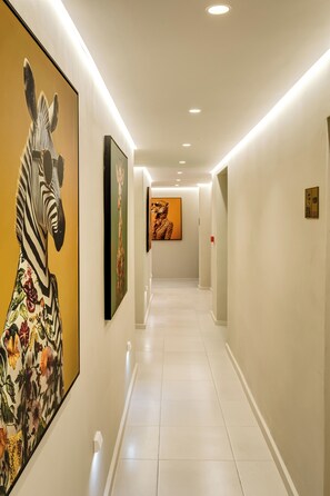 Corredor de hotel com obras de arte nas paredes, incluindo uma pintura de chita e uma placa de número.