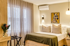 Quarto de hotel com cama, escrivaninha, cadeira, ar condicionado e luminária na parede.