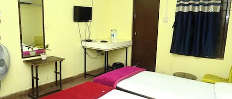 Quarto com cama, escrivaninha, espelho, televisão e janela com cortinas.