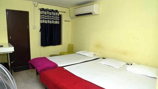 Quarto com duas camas, uma escrivaninha, uma cadeira, ar condicionado e uma porta.