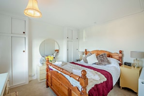 Quarto com cama de madeira, mesas de cabeceira, um espelho e luminária suspensa.