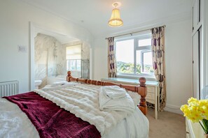 Quarto com cama, janela com cortinas, radiador e área de chuveiro.