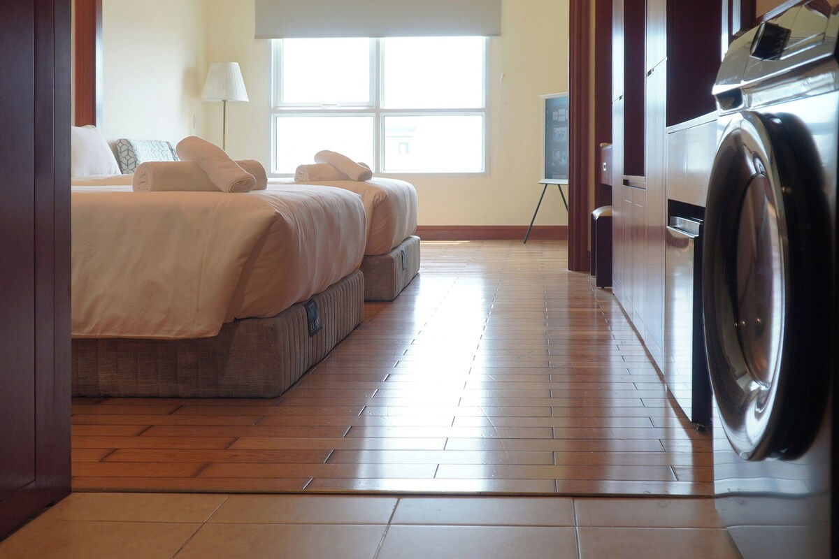 Quarto de hotel com cama, máquina de lavar e janela.