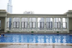 Piscina interior com água cristalina, rodeada por grandes janelas e vista para edifícios altos.