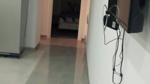 Um corredor com geladeira, televisão fixada na parede e porta que dá para outro quarto.
