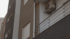 Um edifício com vários andares, varandas, aparelhos de ar condicionado e uma cerca branca em primeiro plano.