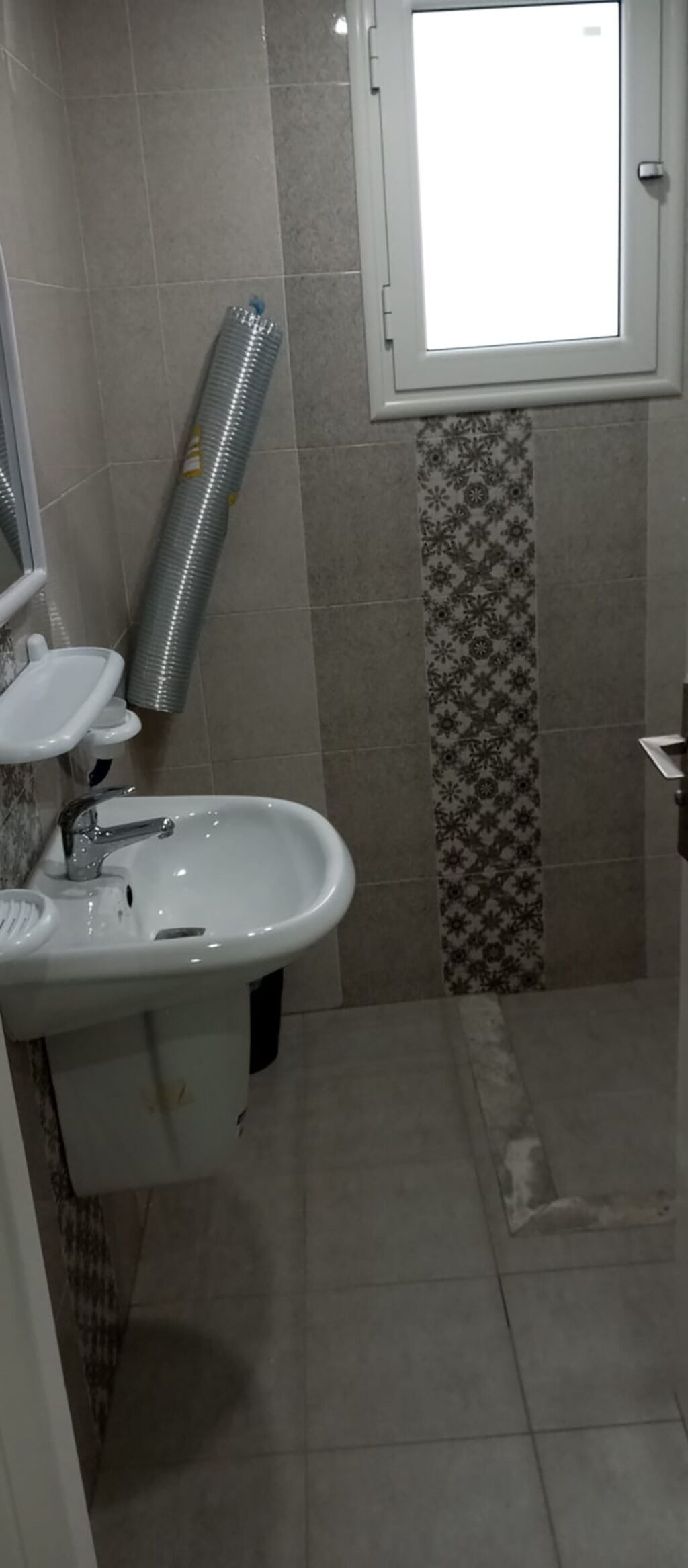 Casa de banho com uma pia branca, espelho e janela.
