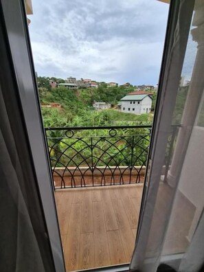 Varanda com piso de madeira e guarda-corpo metálico, com vista para uma área residencial com casas e vegetação.