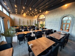 Um restaurante com várias mesas e cadeiras, paredes de tijolo e plantas em vasos.
