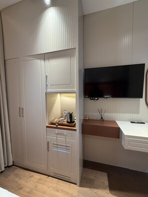 Quarto moderno com guarda-roupa, televisão de tela plana e pequena área de trabalho.