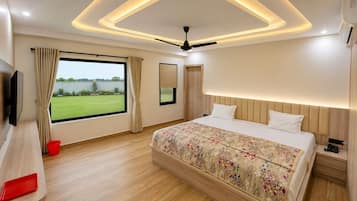 Quarto com cama, televisão, janela com cortinas, ventilador de teto e vista para uma paisagem verde.